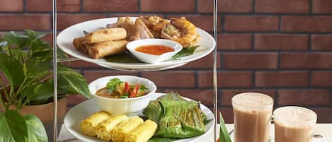 Uma bandeja escalonada com diversos pratos, incluindo comidas fritas, uma tigela de sopa e um prato com comida embalada, com um fundo de parede de tijolos.