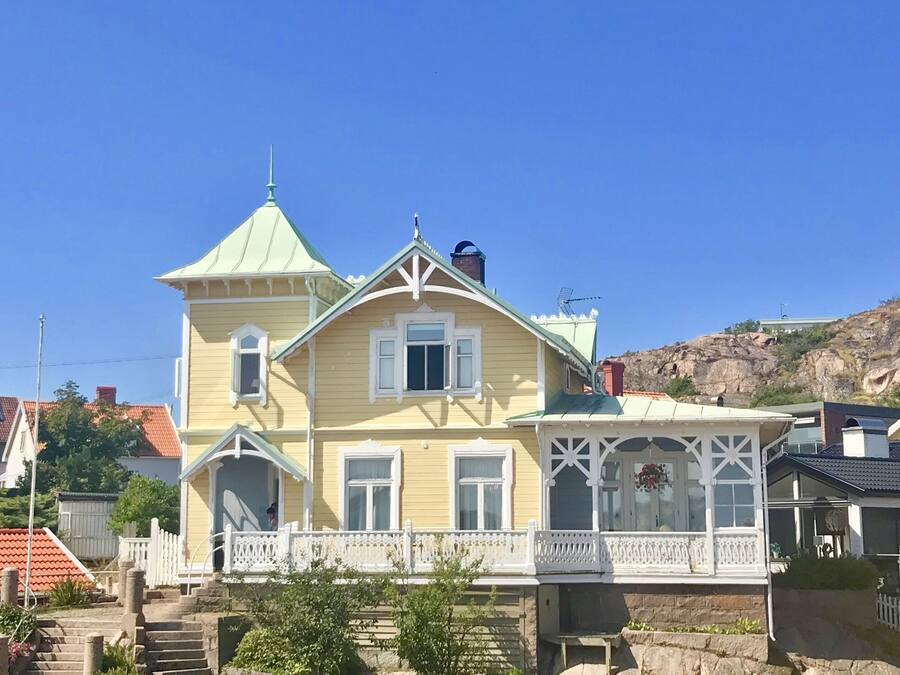 Uma casa de dois andares com telhado verde, detalhes brancos e uma varanda com guarda-corpo branco.