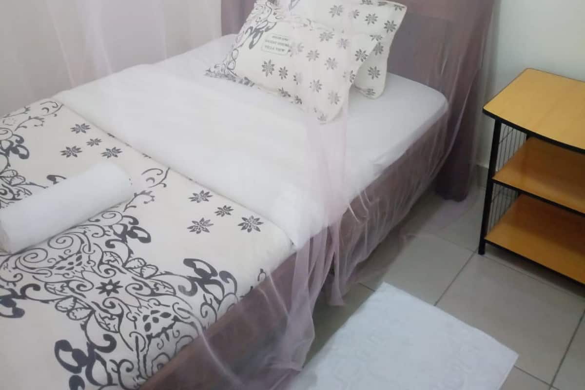 Uma cama bem arrumada com dossel, uma mesa de cabeceira e uma pequena prateleira de madeira.