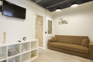 Uma sala de estar moderna com televisão de tela plana, um sofá marrom, uma estante branca com copos e um painel de parede de tijolos.