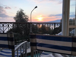 Uma varanda com cadeiras listradas, um poste de luz e vista para o pôr do sol.