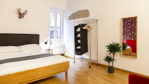 Quarto com cama, mesa de cabeceira, abajur, varal de roupa, planta em vaso e espelho na parede.