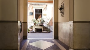 Corredor que leva a um pátio com lareira, plantas em vasos e piso de azulejos.