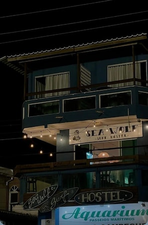 Um edifício de dois andares com uma placa que diz 'Sea Wolf Surf Hostel' e outra placa abaixo com a inscrição 'Aquarium Passeios Marítimos'.