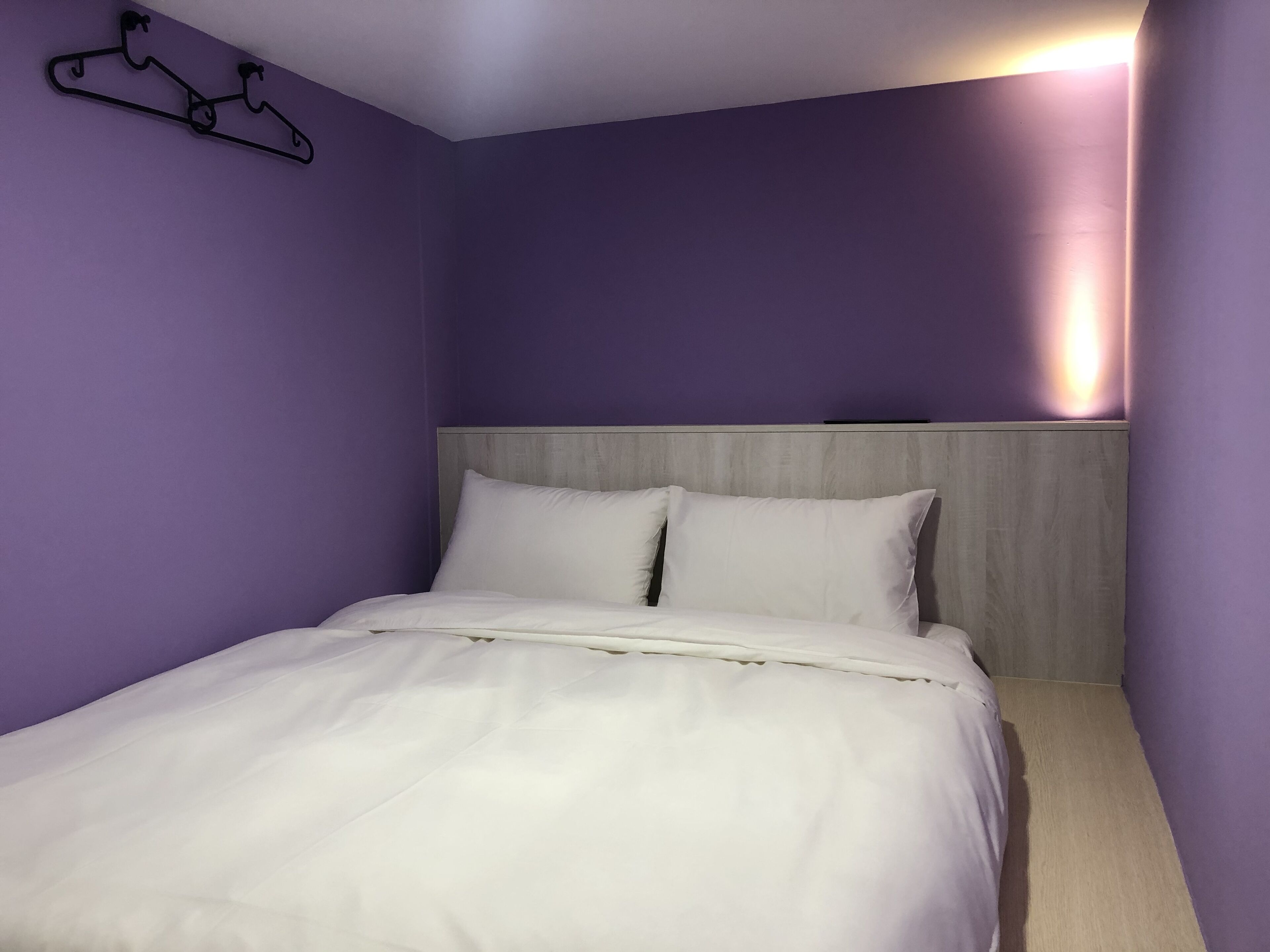 Cama bem arrumada em quarto com paredes roxas e cabeceira de madeira.