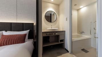 Quarto de hotel com cama, banheiro com pia, espelho e banheira.