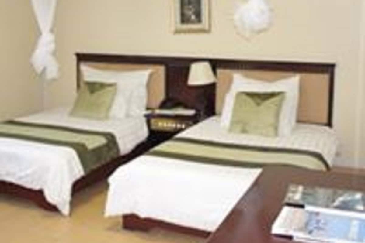 Quarto de hotel com duas camas, cada uma com dossel, uma mesa de cabeceira, um abajur e um quadro na parede.