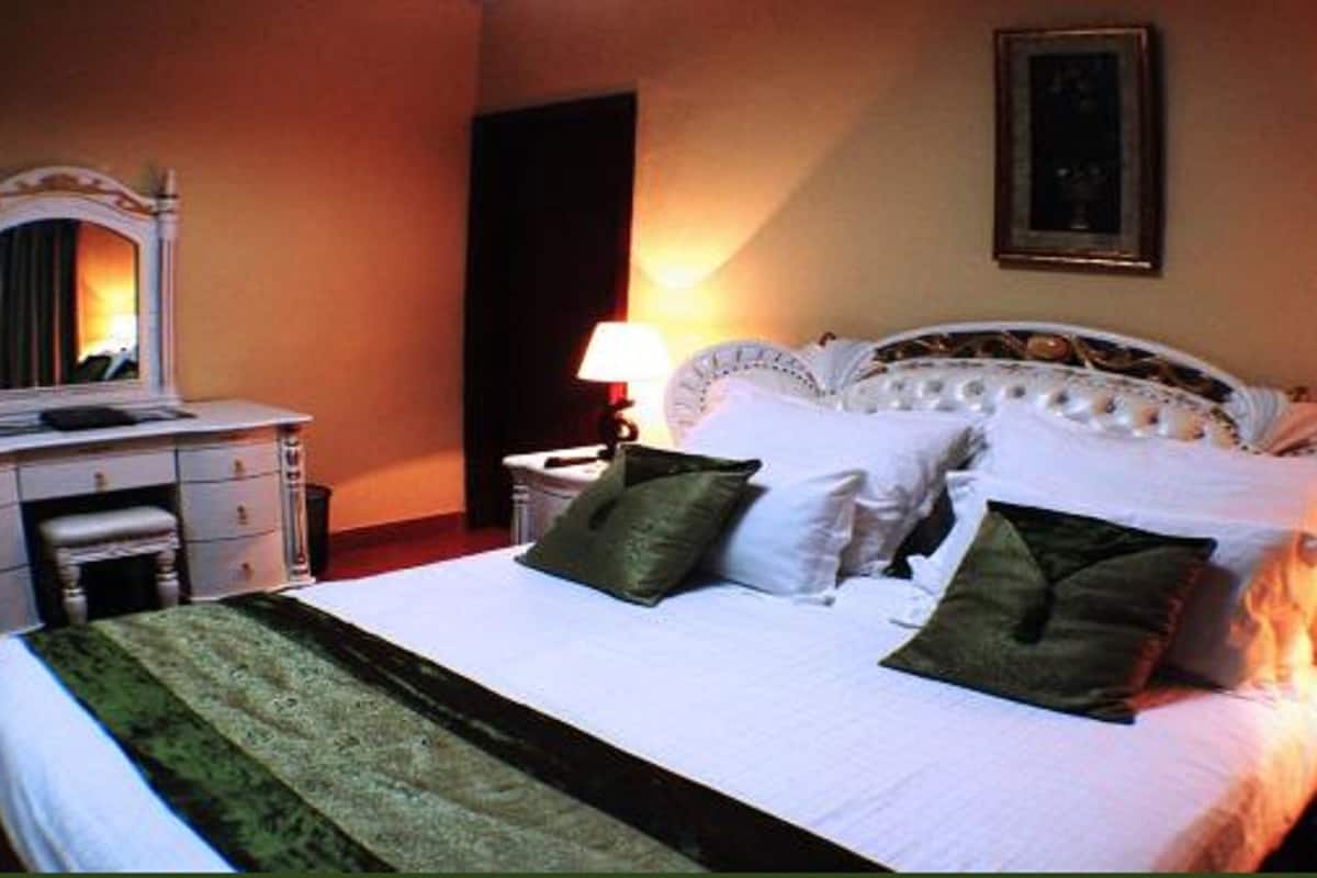 Quarto com cama, penteadeira, espelho, abajur e quadro na parede.