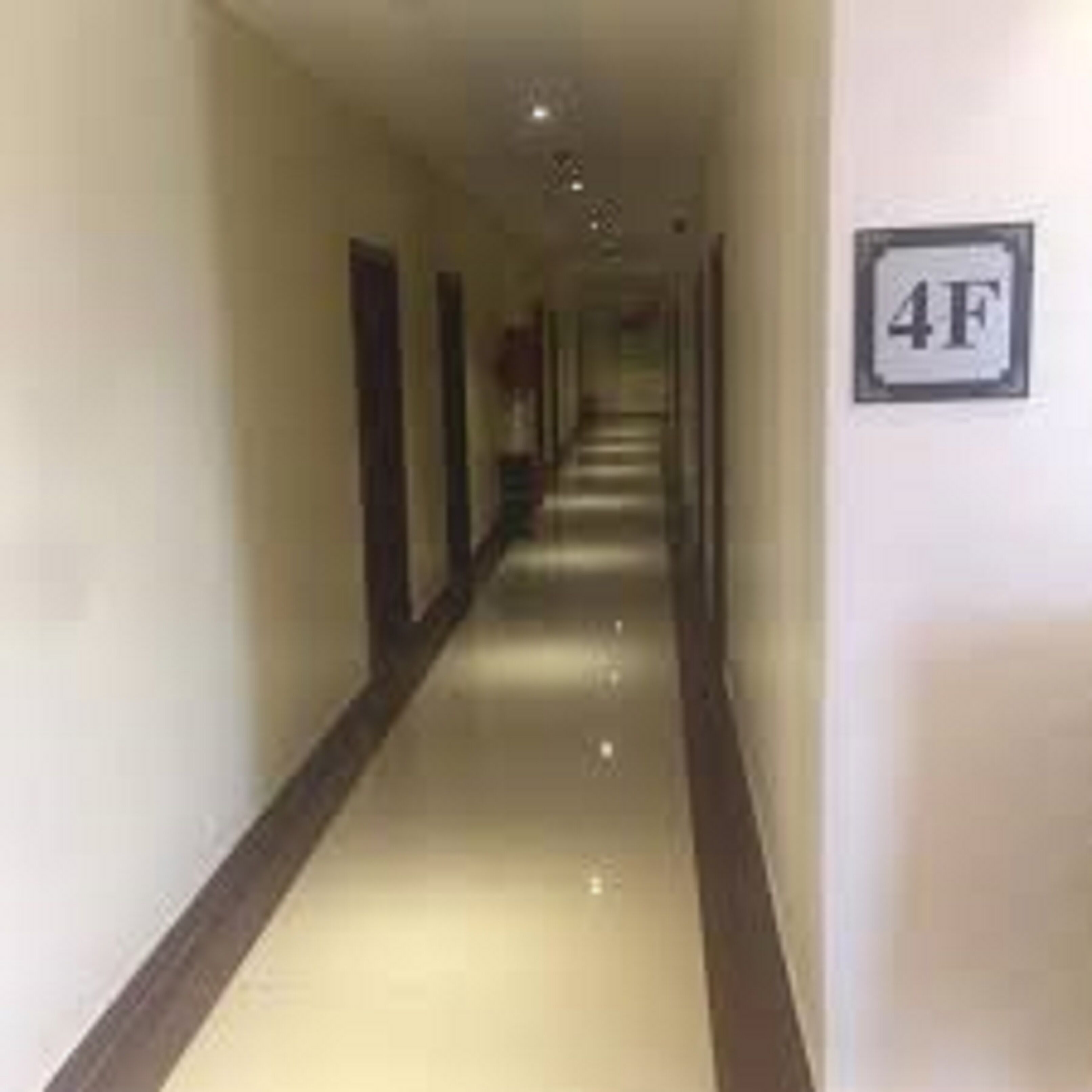 Um corredor comprido e estreito, com piso lustroso e portas de um lado. Uma placa com a inscrição '4F' é visível na parede.