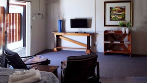 Um quarto com escrivaninha de madeira, televisão, estante e uma cadeira.