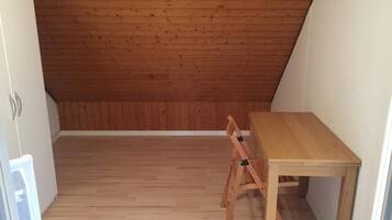 Um pequeno quarto no sótão com teto de madeira inclinado, uma mesa de madeira e uma cadeira.