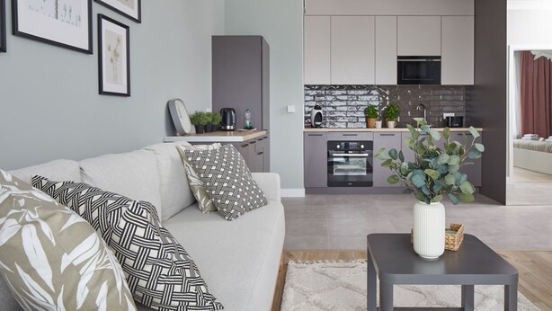 Uma sala de estar moderna com sofá, uma mesinha de centro e uma cozinha ao fundo.