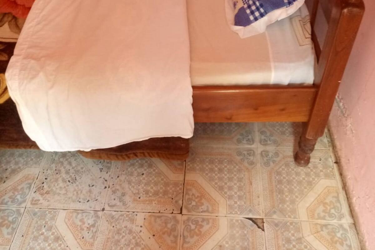 Quarto pequeno com cama de casal e estrutura de madeira, parede rosa.
