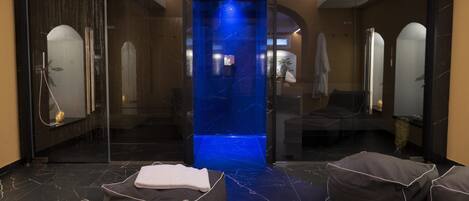 Um spa moderno com divisória de vidro, elemento aquático iluminado em azul e áreas de estar confortáveis.