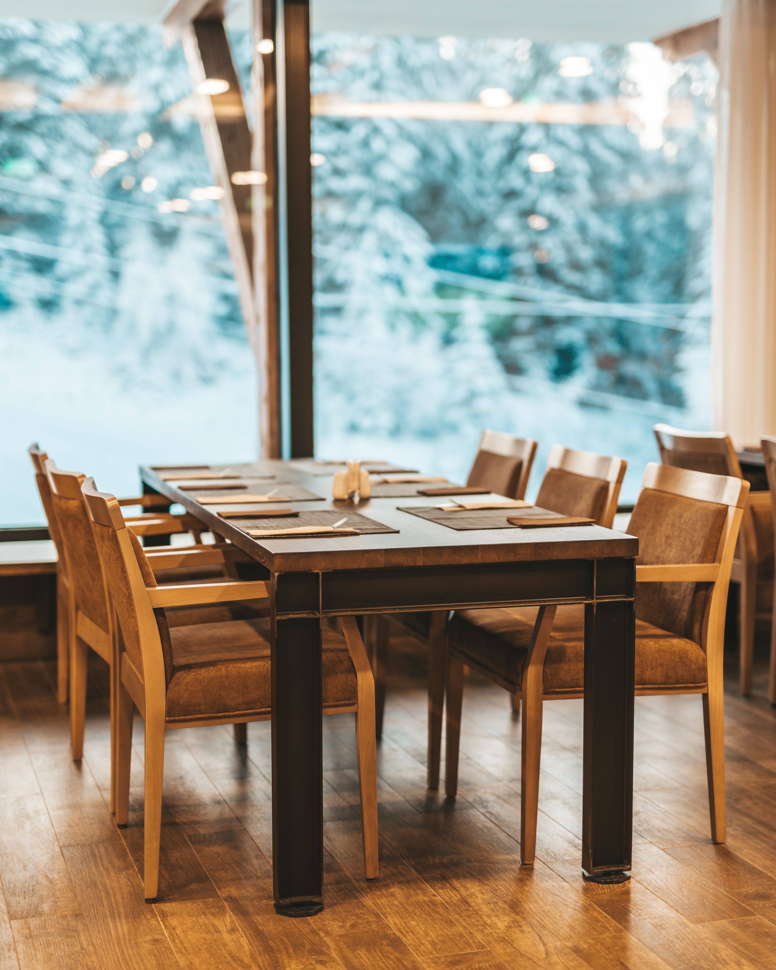 Uma área de refeições com mesa e cadeiras de madeira, grandes janelas com vista para árvores e design de interiores moderno.