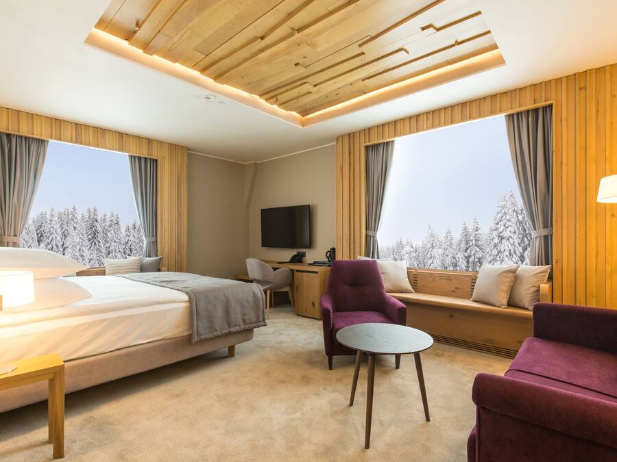 Quarto de hotel com cama, escrivaninha, cadeira, sofá e televisão.