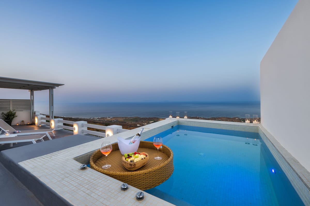 Uma área na piscina com vista para o oceano, uma cesta de vime com comida e bebidas, e espreguiçadeiras.