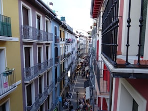 Uma rua estreita com edifícios altos, varandas e uma passarela para pedestres.