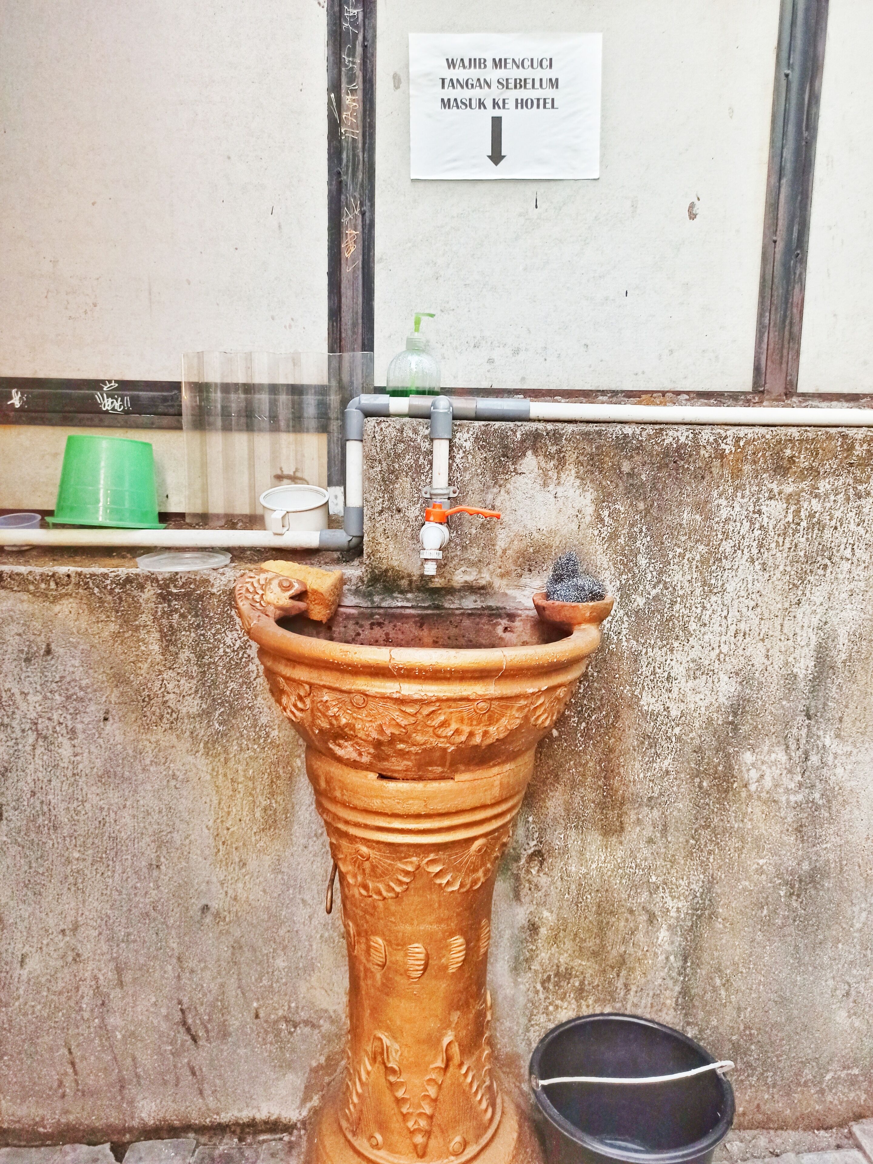 Uma fonte de água em terracota com uma placa em cima.