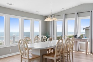 Uma sala de jantar com uma mesa grande, cadeiras e vista para o oceano.
