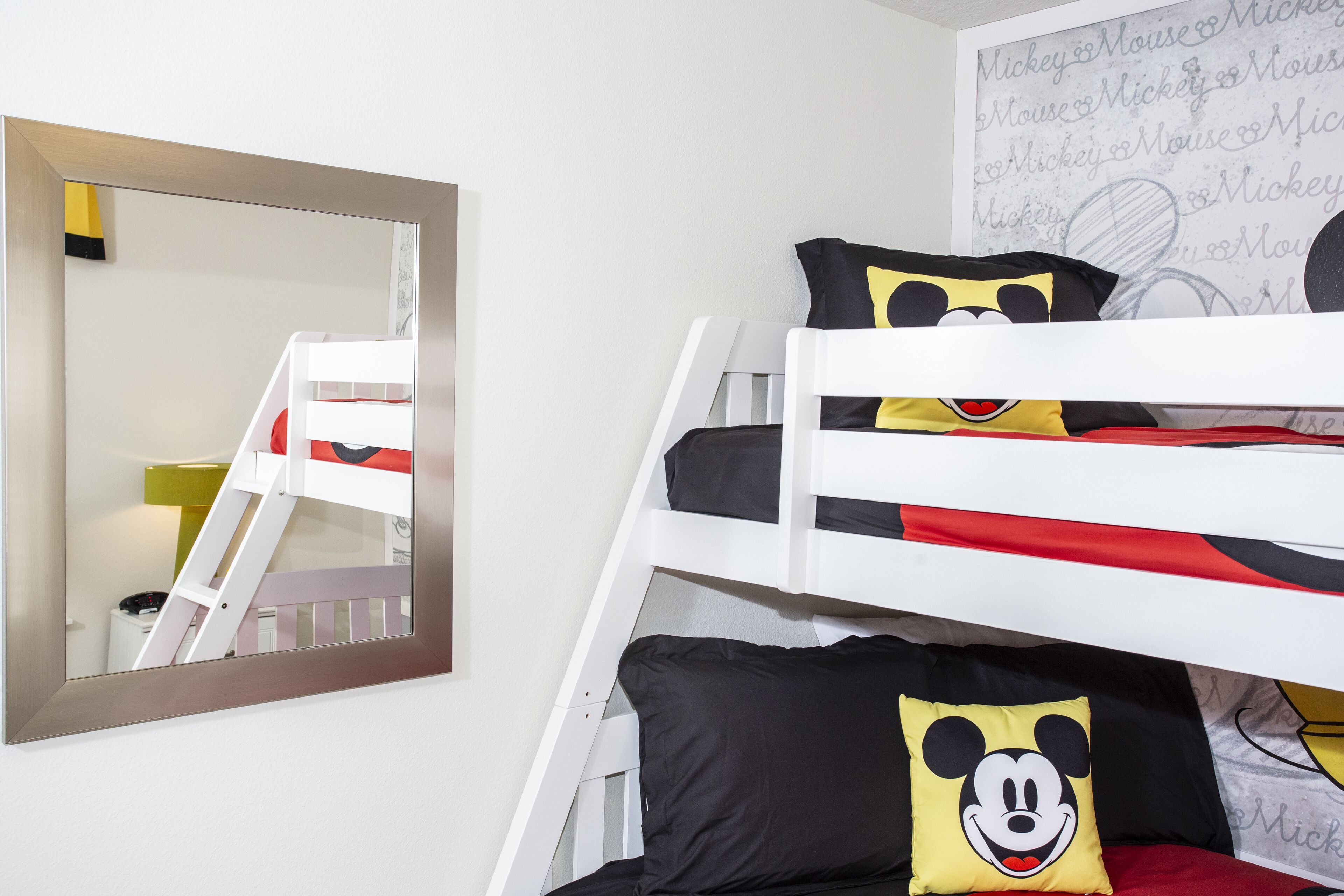 Uma cama de solteiro com almofadas do Mickey Mouse, um espelho e um painel com a inscrição Mickey Mouse.