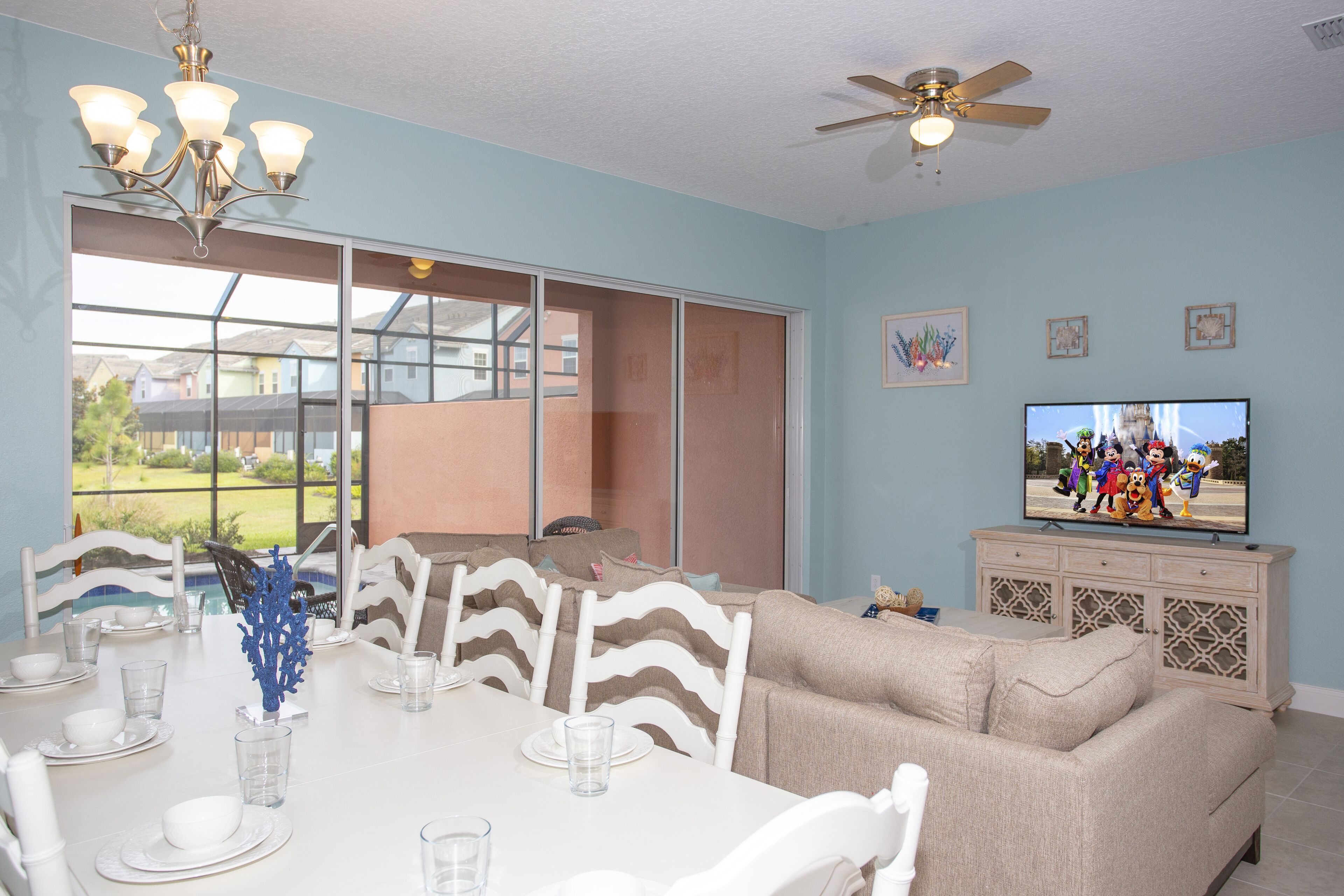 Uma sala de jantar com uma mesa posta para quatro pessoas, um ventilador de teto e uma televisão em um móvel de madeira.