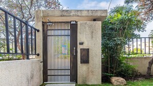 Entrada murada com muro de concreto, portão de metal e um pequeno caminho que leva a uma área gramada.
