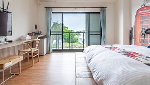 Quarto com uma cama grande, uma mesa com cadeira, uma TV e um telefone vermelho decorativo.