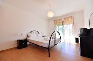 Quarto com cama, mesas de cabeceira, televisão e janela com cortinas.