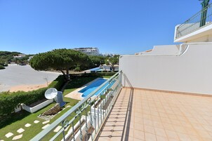 Uma varanda com vista para uma piscina, uma antena parabólica e um espaço pavimentado com uma árvore.