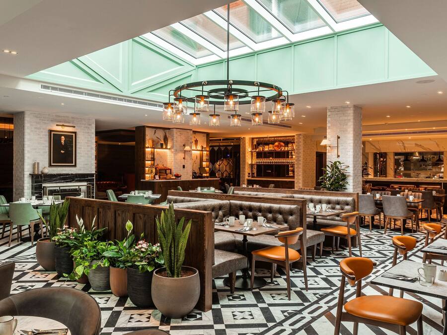 Um restaurante moderno com teto alto, um lustre central e uma variedade de opções de assentos, incluindo cabines e mesas.