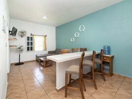 Uma sala de jantar com uma mesa comprida, quatro cadeiras, um banco e um dispensador de água.