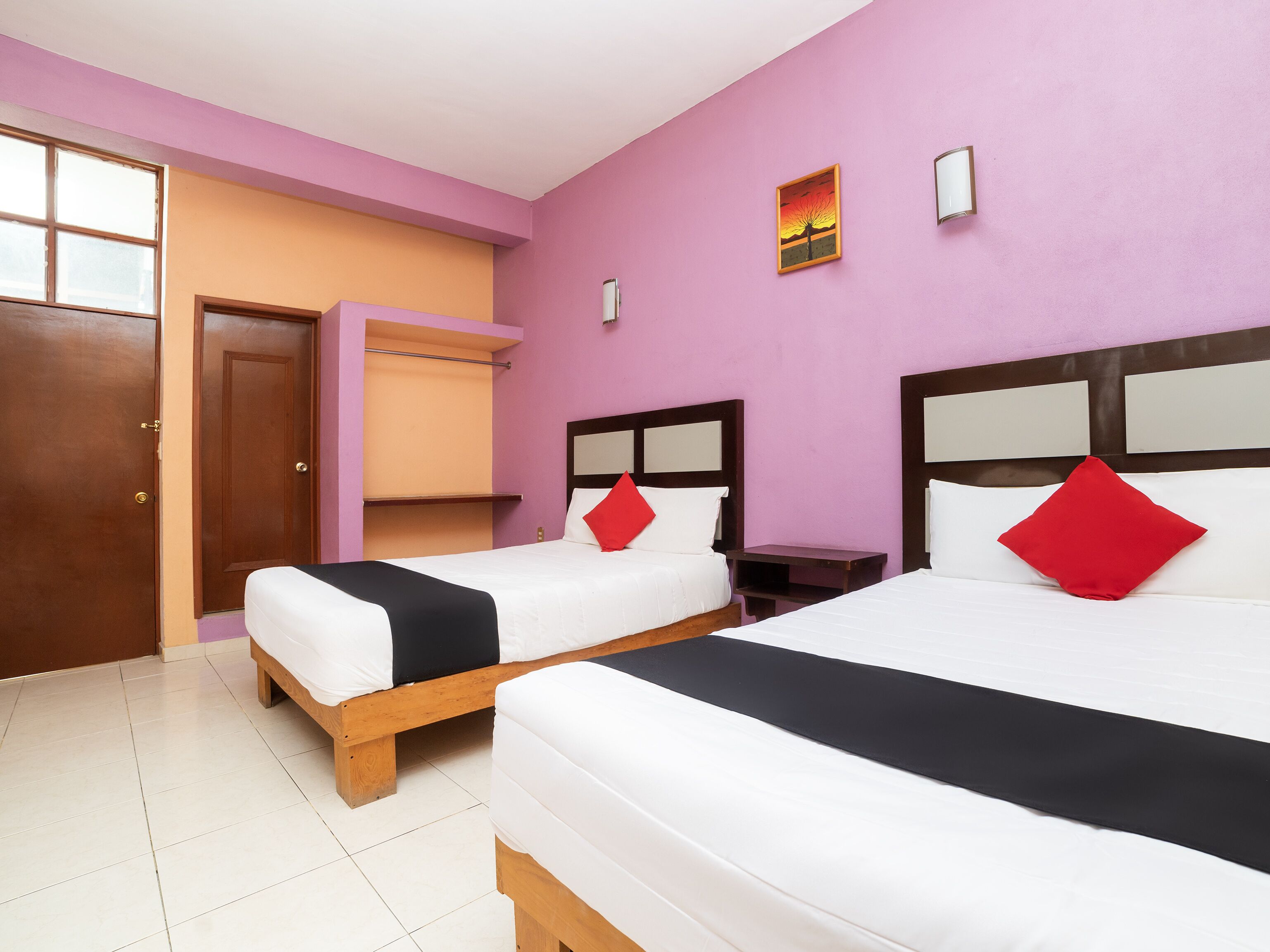 Quarto de hotel com duas camas, um guarda-roupa de madeira, uma janela e um quadro na parede.