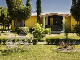 Um edifício amarelo com varanda, rodeado por jardins bem cuidados e árvores.