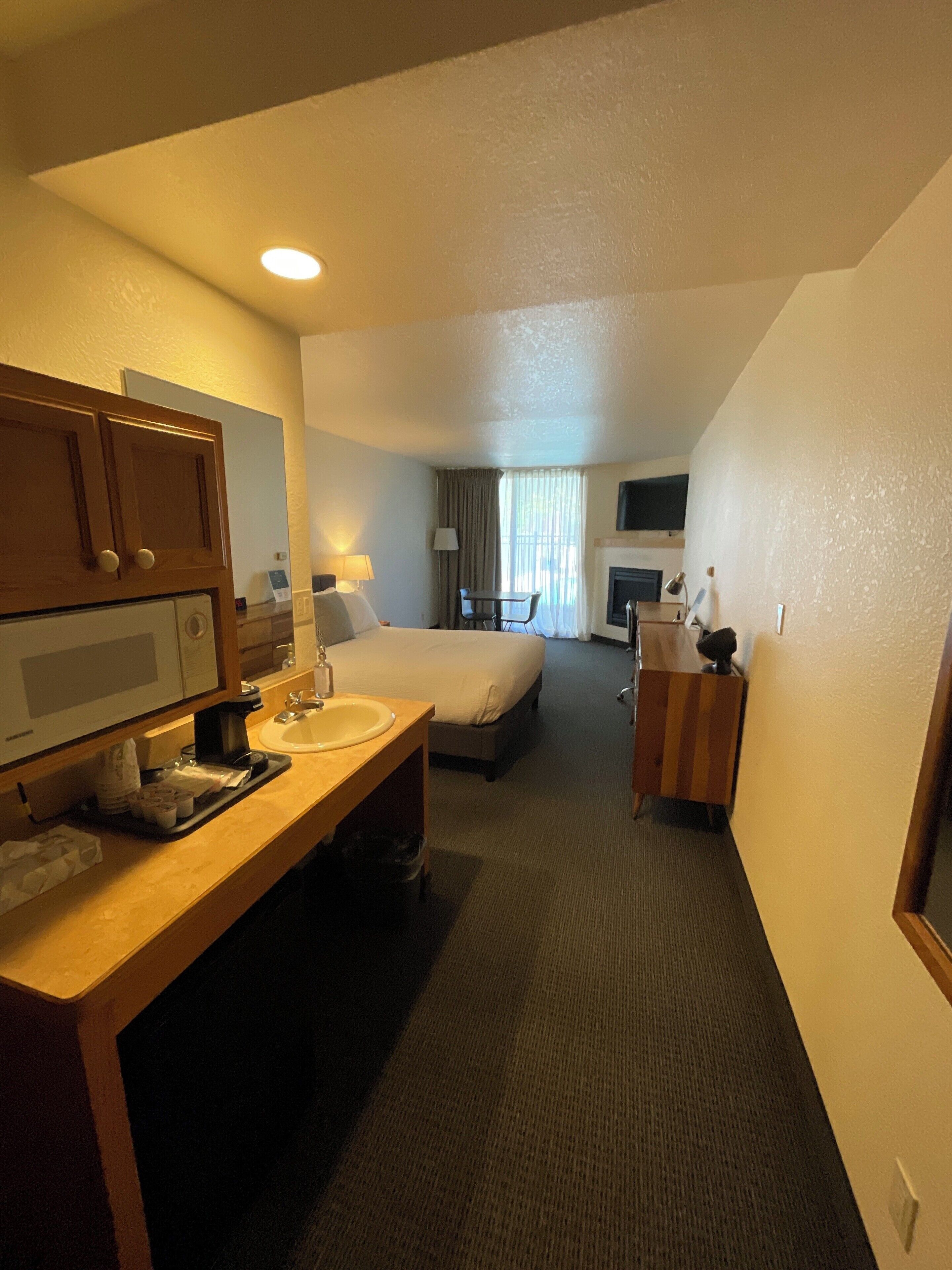 Quarto de hotel com cama, secretária, computador, cadeira, mesa pequena e televisão.