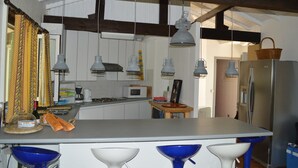 Cozinha com ilha central, luminárias pendentes, frigorífico e micro-ondas.