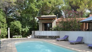 Piscina com espreguiçadeiras, um pequeno edifício com telhado em azulejos e vegetação exuberante.
