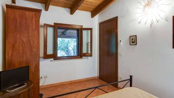 Quarto com cama, televisão em suporte, janela com vista para árvores e porta.