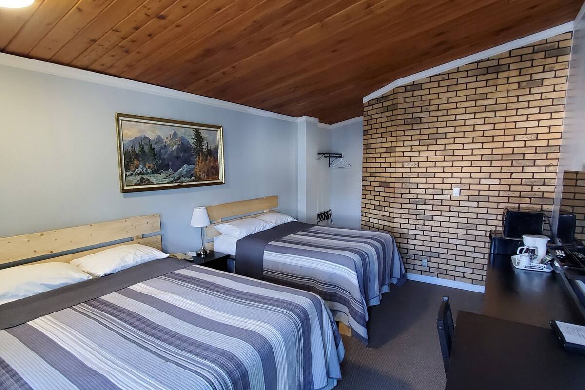 Quarto com três camas, uma escrivaninha, um computador e uma parede de tijolos.