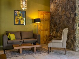 Uma sala de estar com um sofá, uma poltrona, uma mesa de centro, um abajur e um quadro na parede.