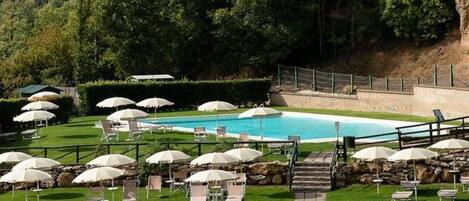Uma área de piscina com espreguiçadeiras e guarda-sóis, cercada por paredes de pedra e vegetação.