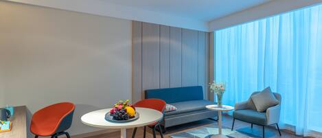 Uma sala de estar moderna com sofá, cadeiras, uma mesinha com frutas e uma janela grande com cortinas.