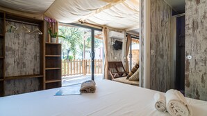 Quarto com cama, guarda-roupa de madeira, televisão e porta de vidro deslizante para área externa.