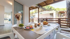 Uma mesa de jantar com itens de café da manhã, um vaso com flores secas e vista para uma área residencial.