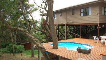 Um deck de madeira com piscina, churrasqueira e um pequeno galpão.