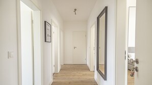 Um corredor com piso de madeira, paredes brancas e portas que dão para quartos.