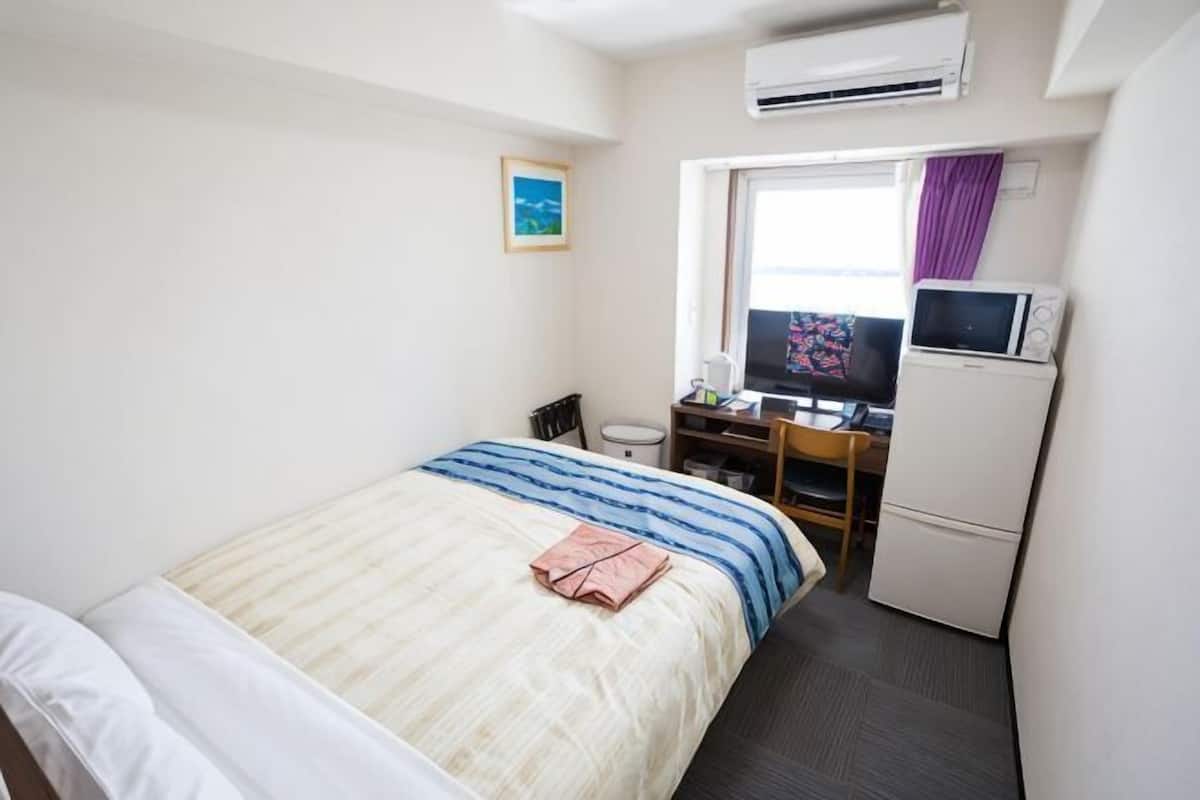 Quarto de hotel com cama, escrivaninha com computador, frigorífico e janela com cortinas.