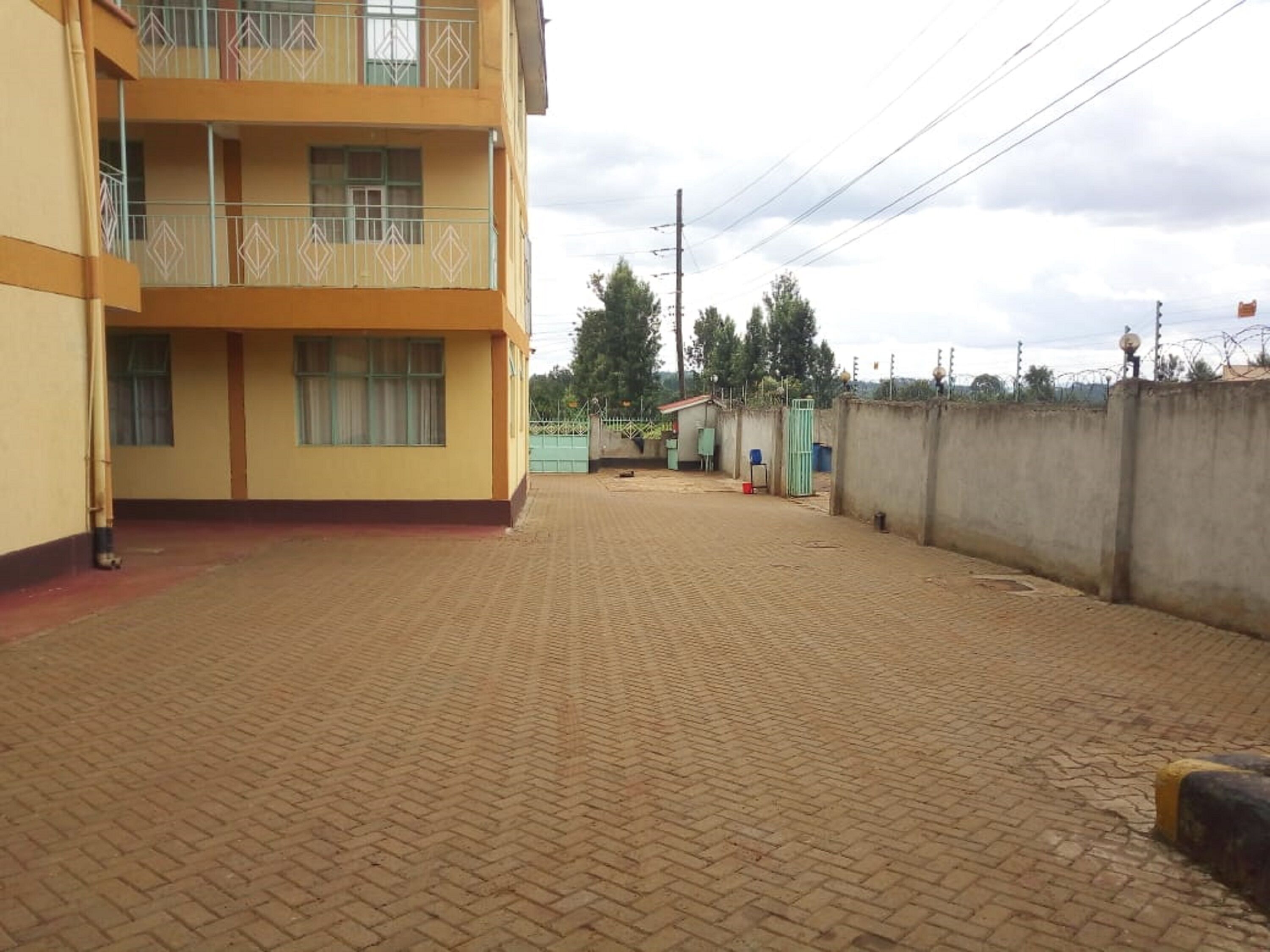 Um edifício com fachada amarela, pátio pavimentado e portão.