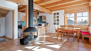 Uma sala de estar ampla com uma lareira grande, vigas de madeira, cozinha e área de refeições com vista para as montanhas.