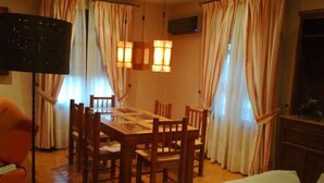Uma área de refeições com uma mesa e cadeiras de madeira, cortinas e uma televisão fixada na parede.